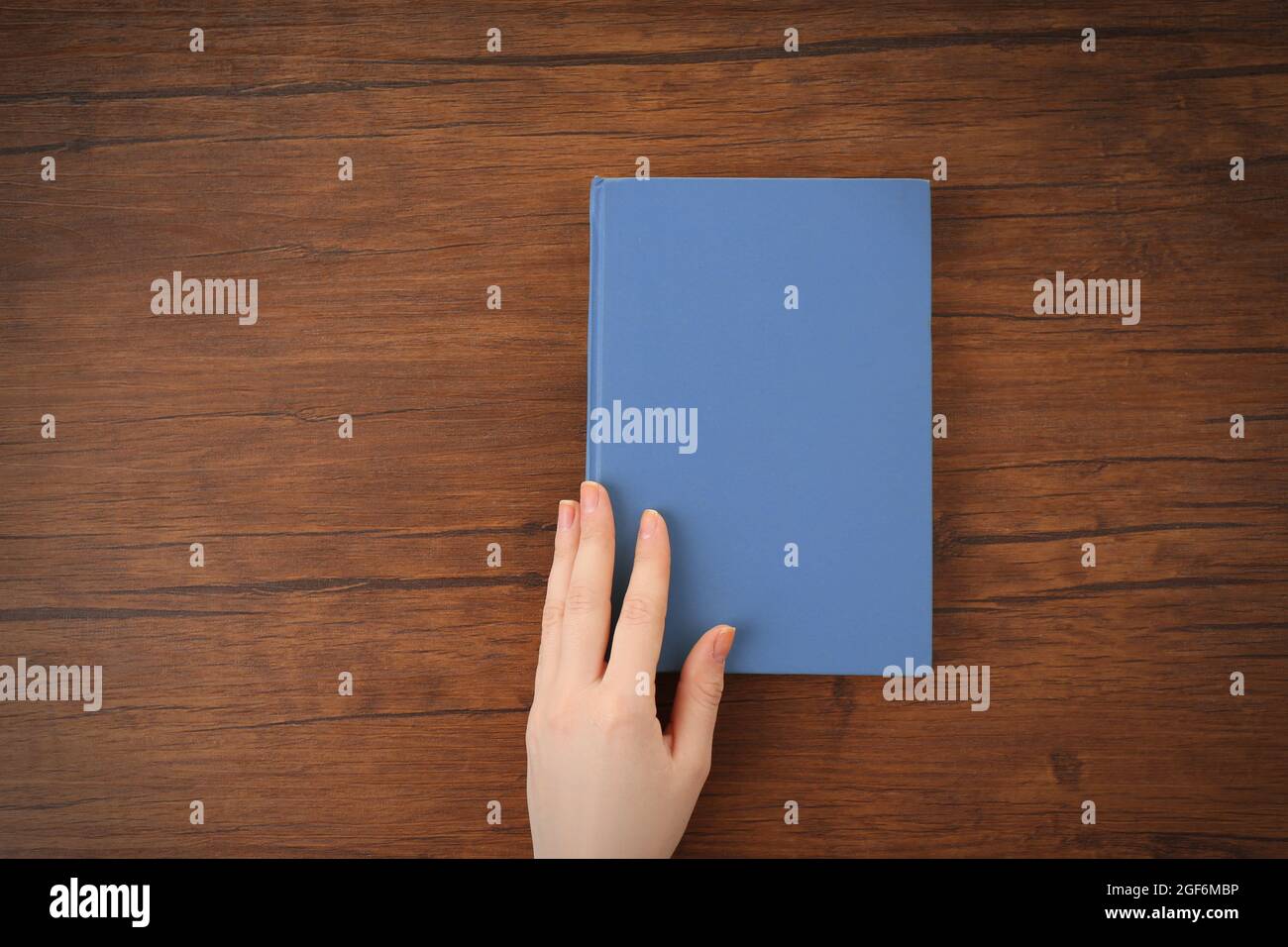 Female hand holding a light blue book cover on the brown wooden desk ...