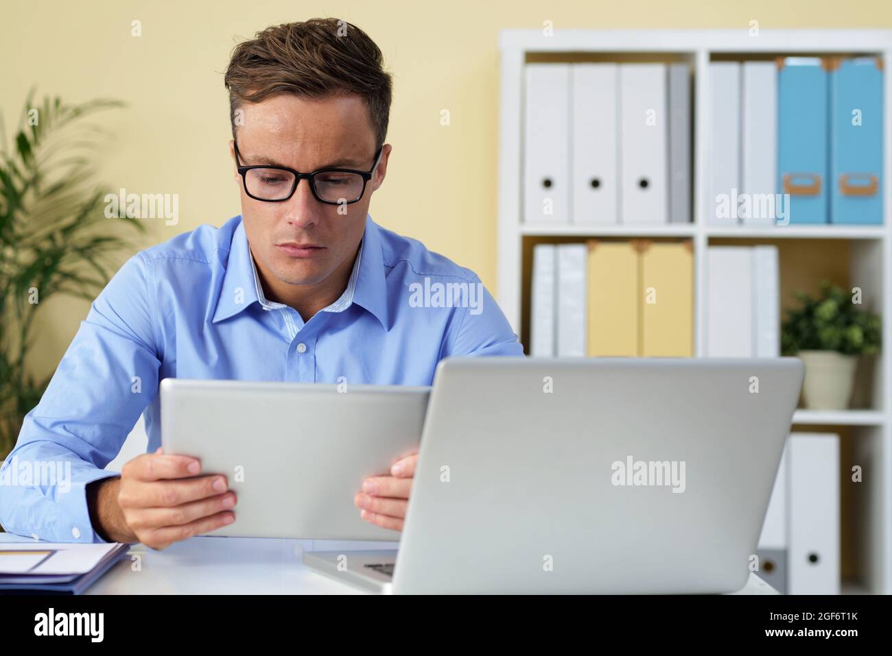 Serious concentrated young businessman in glasses sitting at office ...