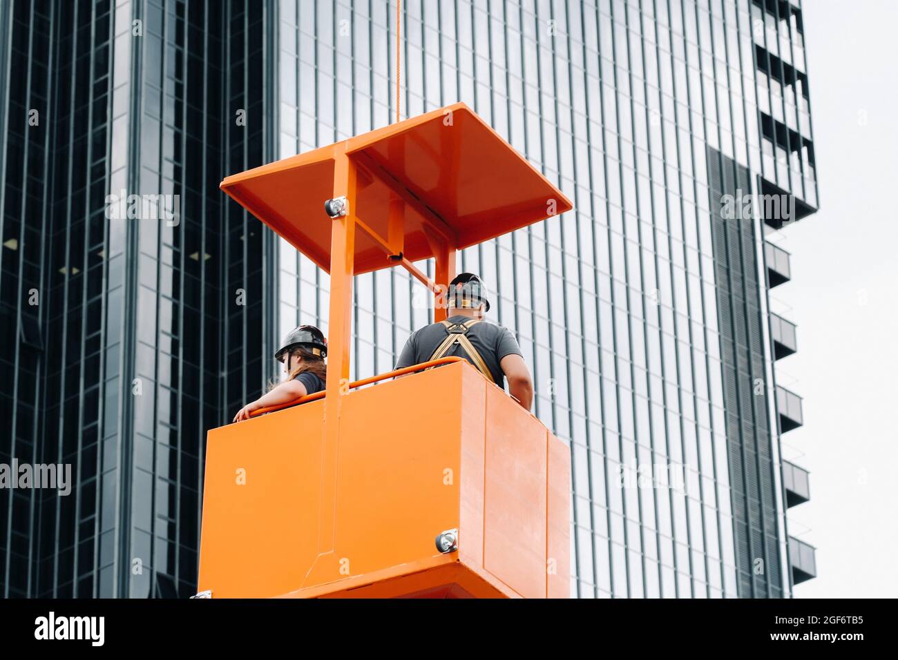 Workers in a construction cradle climb on a crane to a large glass ...