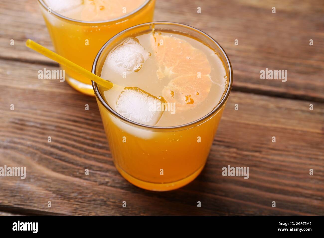 Glasses of orange juice with ice blocks and tubule on wooden background ...