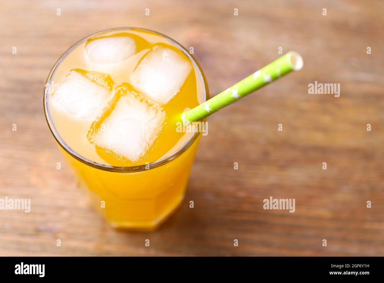 Glass of orange juice with ice blocks and tubule on wooden background ...
