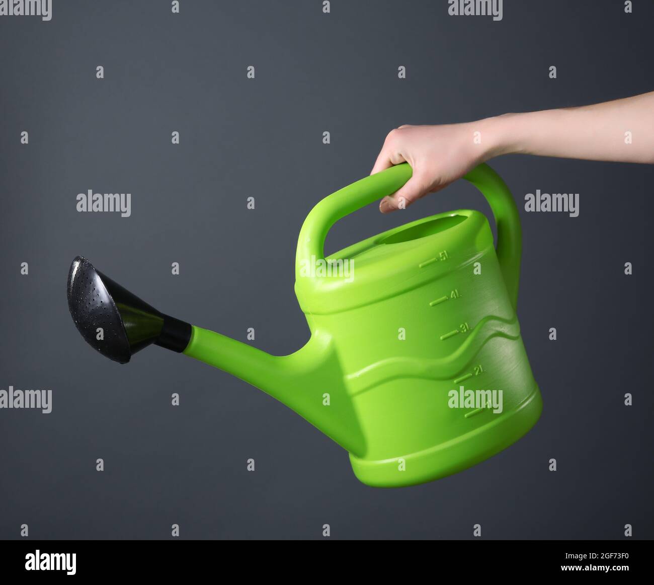 Hand holding green plastic watering can on grey background Stock Photo ...