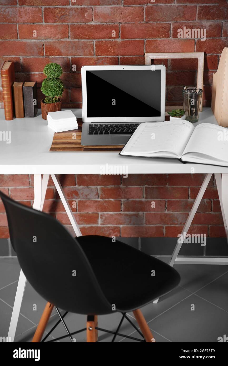 Workplace with laptop, table and chair on brick wall background Stock ...