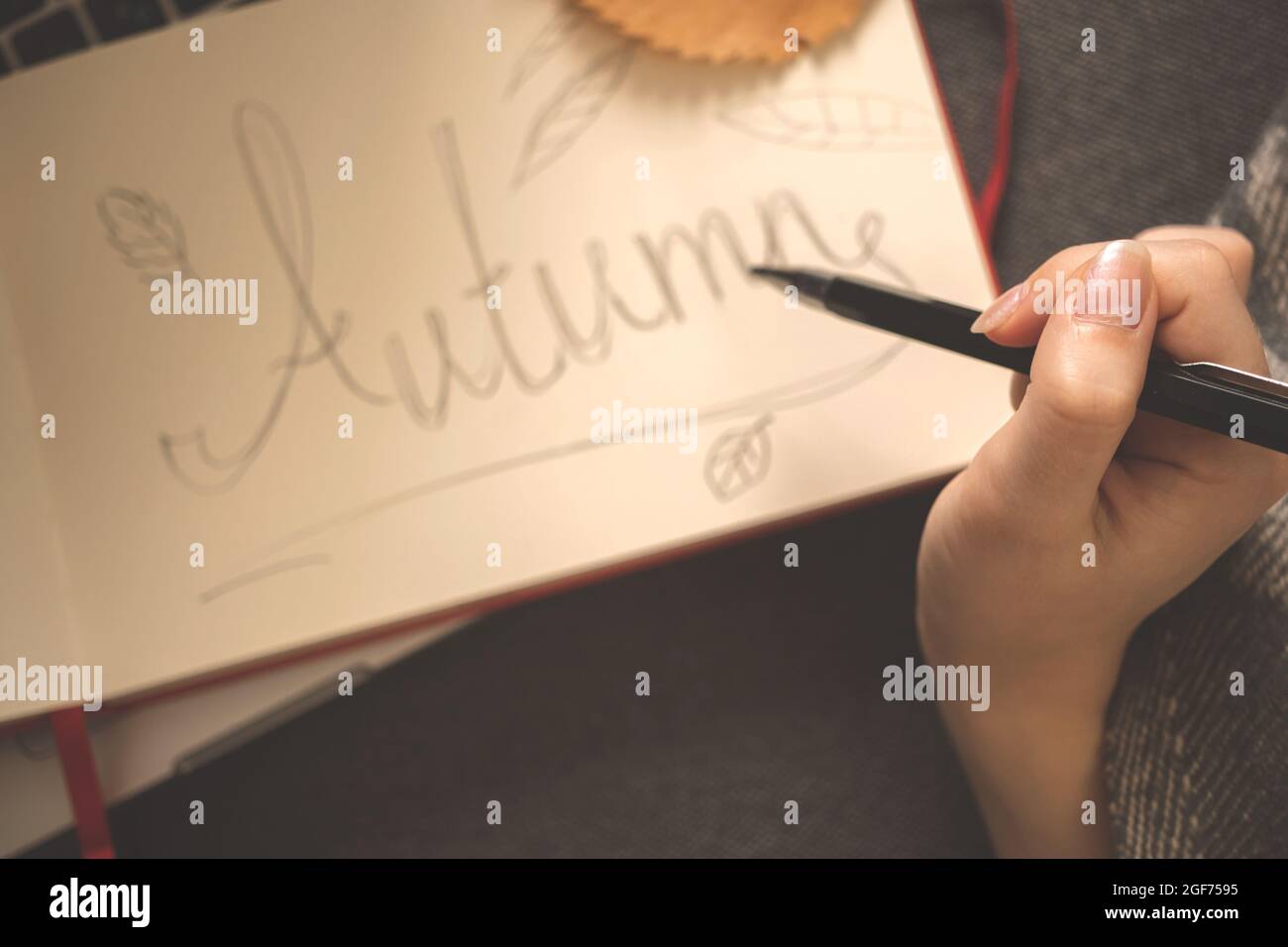 Hand written Autumn word in notepad, cozy home background. Hand with ...