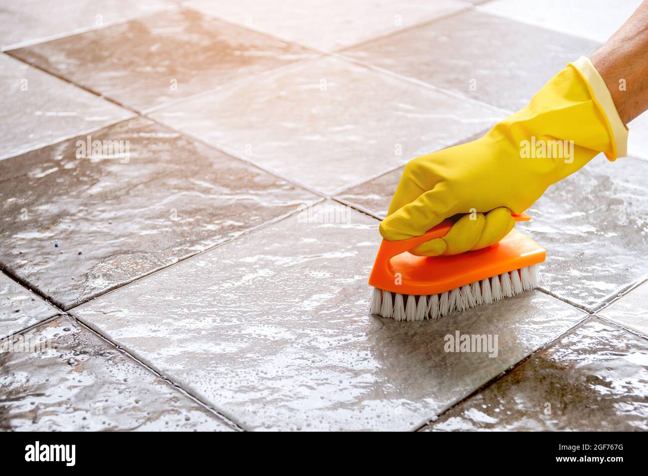 Hands wearing yellow rubber gloves are using a plastic floor scrubber ...