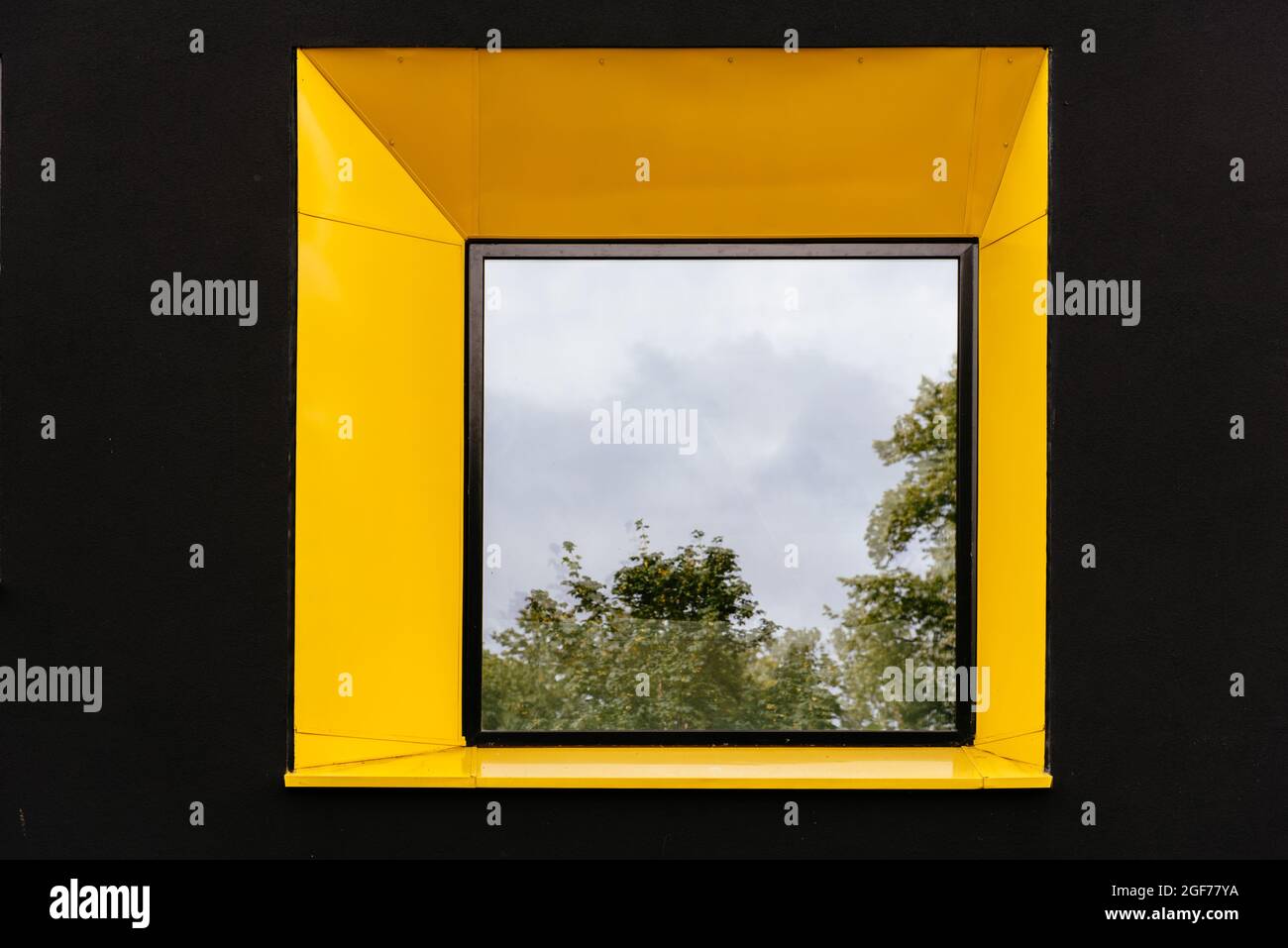 Yellow window on black facade with reflection of green tree on ...