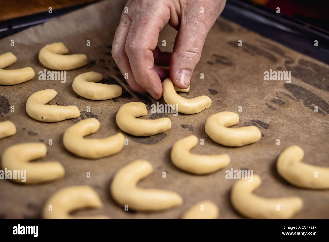 Old female hands placing small vanilla crescent biscuits on tray with ...