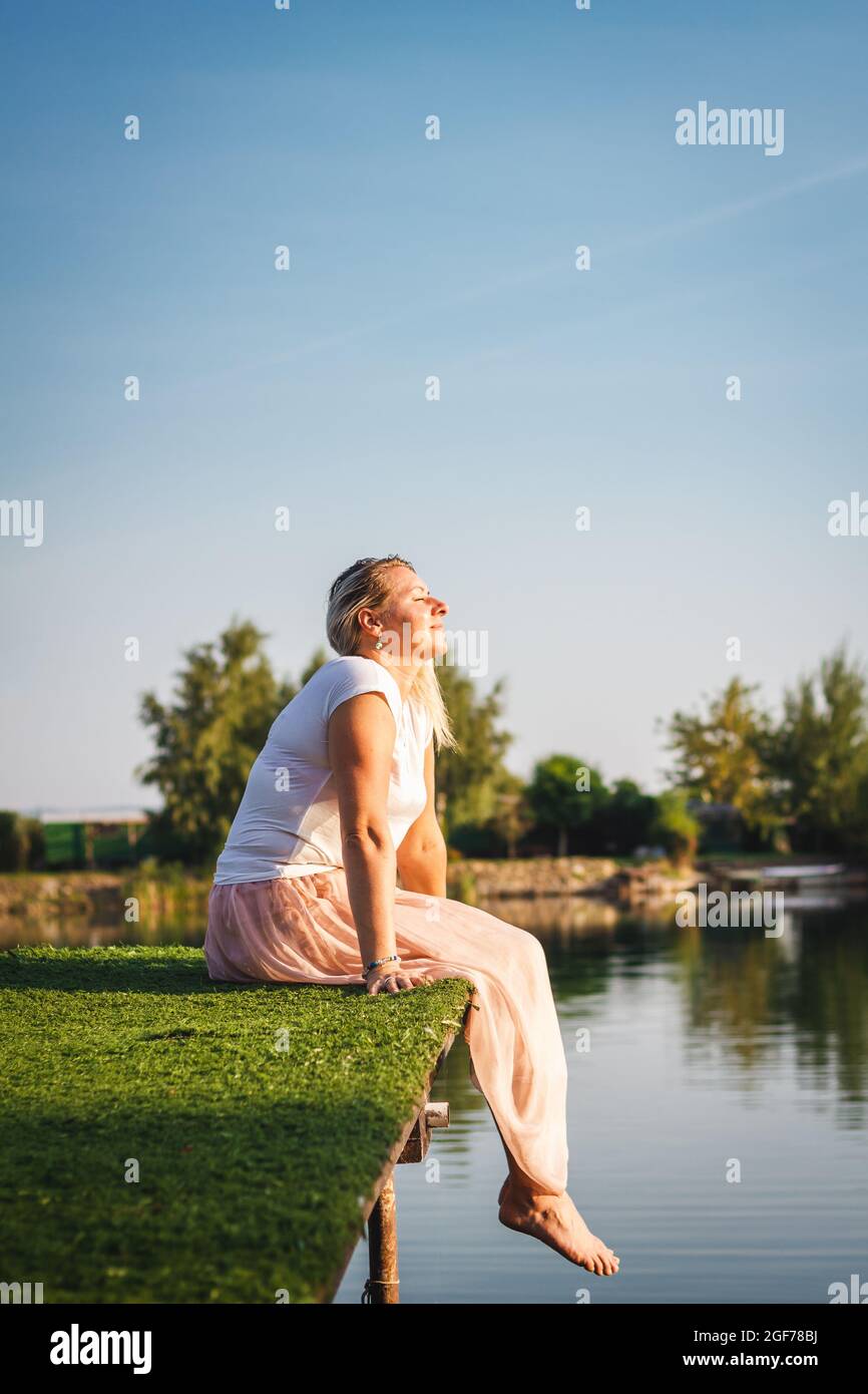 Calm overweight woman sitting on pier by the water and enjoying ...