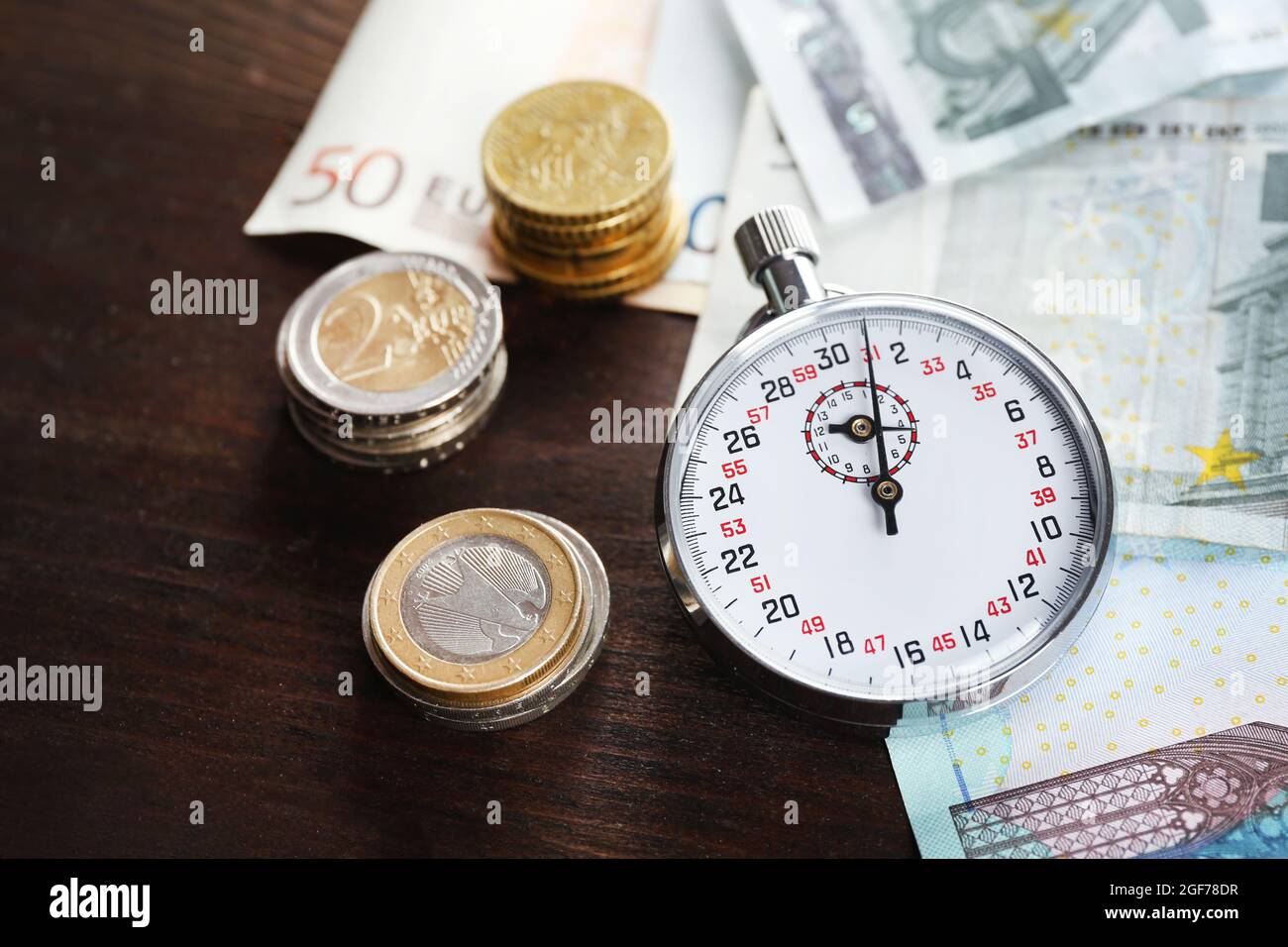 Stopwatch with euro banknotes and coins on wooden background. Time is ...