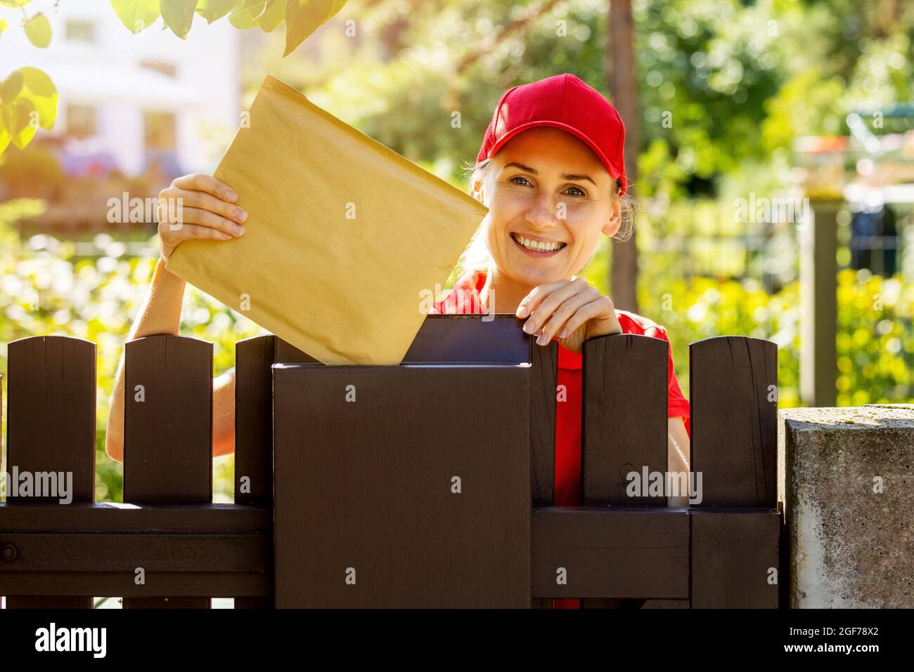smiling postman mail carrier inserting envelope into mailbox Stock ...