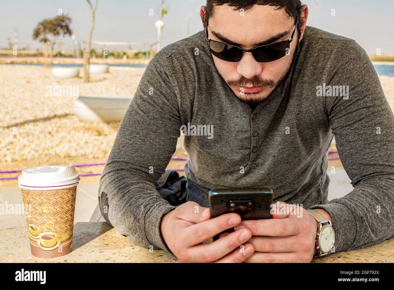 Israeli man with sunglasses using his phone at the beach with a plastic ...