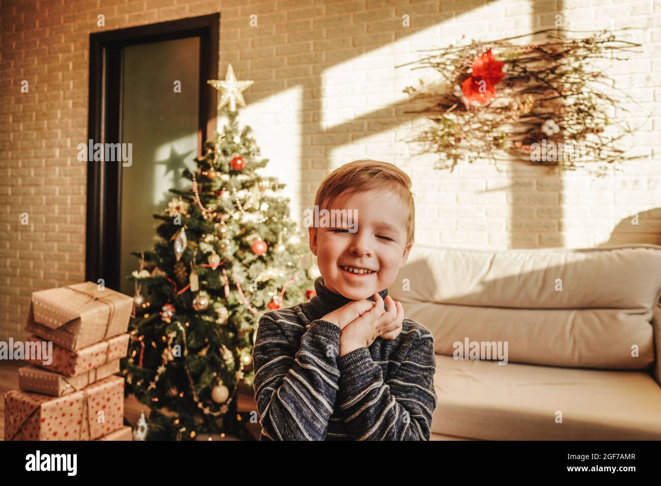 Little boy praying at Christmas Eve, Christmas tree and gift boxes on ...
