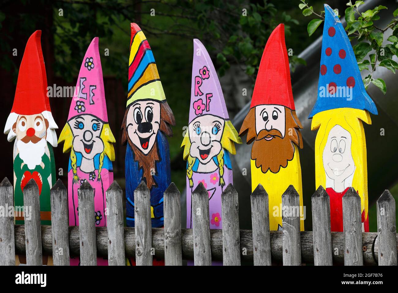 Colourfully painted funny dwarf figures behind wooden fence, Bavaria ...
