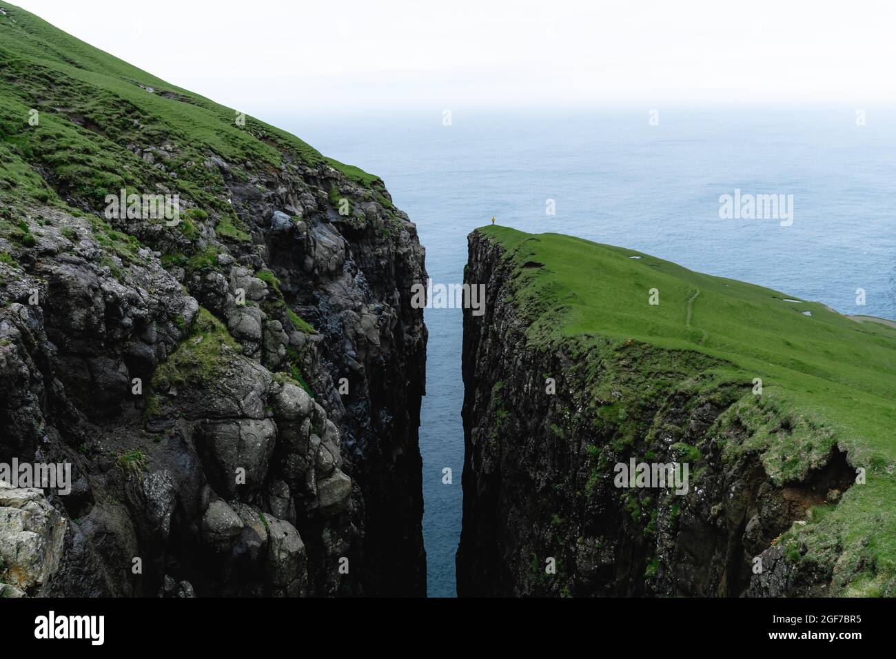 Small person standing on cliff with deep crevice, Sandvik, Suduroy ...
