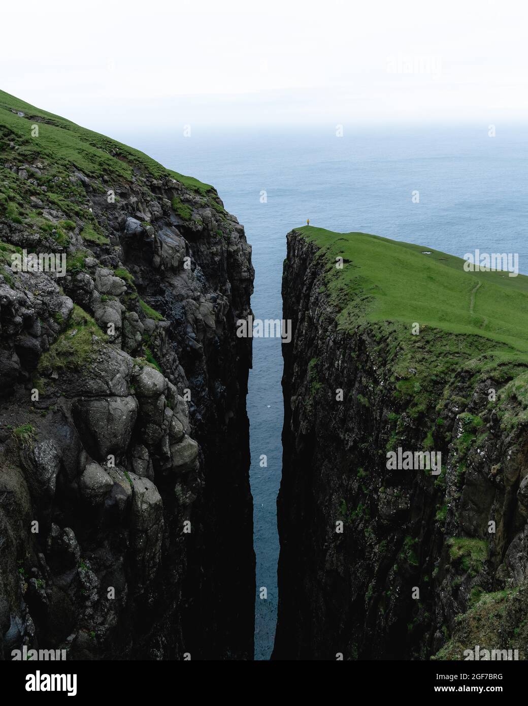 Small person standing on cliff with deep crevice, Sandvik, Suduroy ...