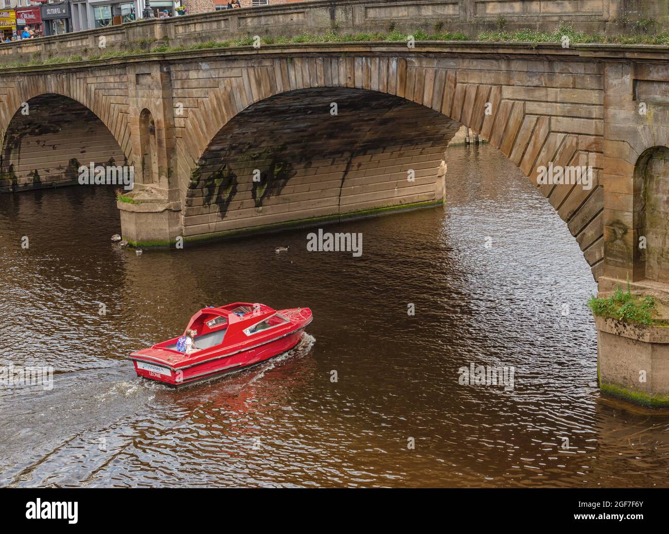 An arch of a 19th century stone bridge spanning a river with a small ...