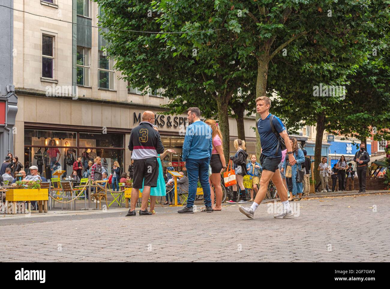 A pedestrian shopping street with people standing, sitting and walking ...