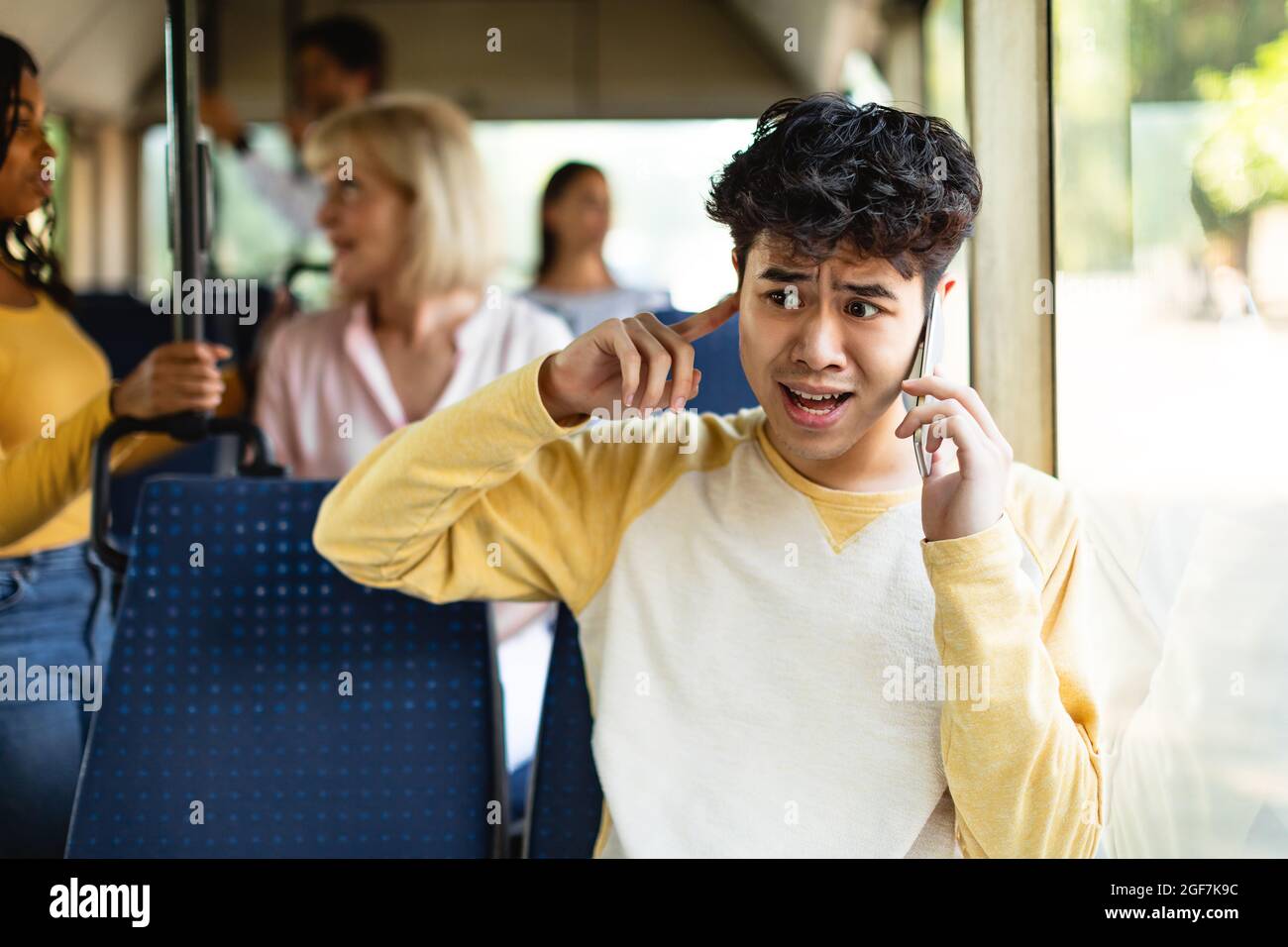 Confused asian guy talking on phone holding finger in ear Stock Photo ...