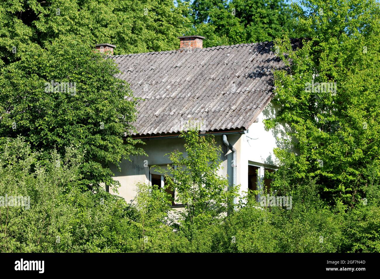 Abandoned small white suburban family house with destroyed windows and broken window blinds ...