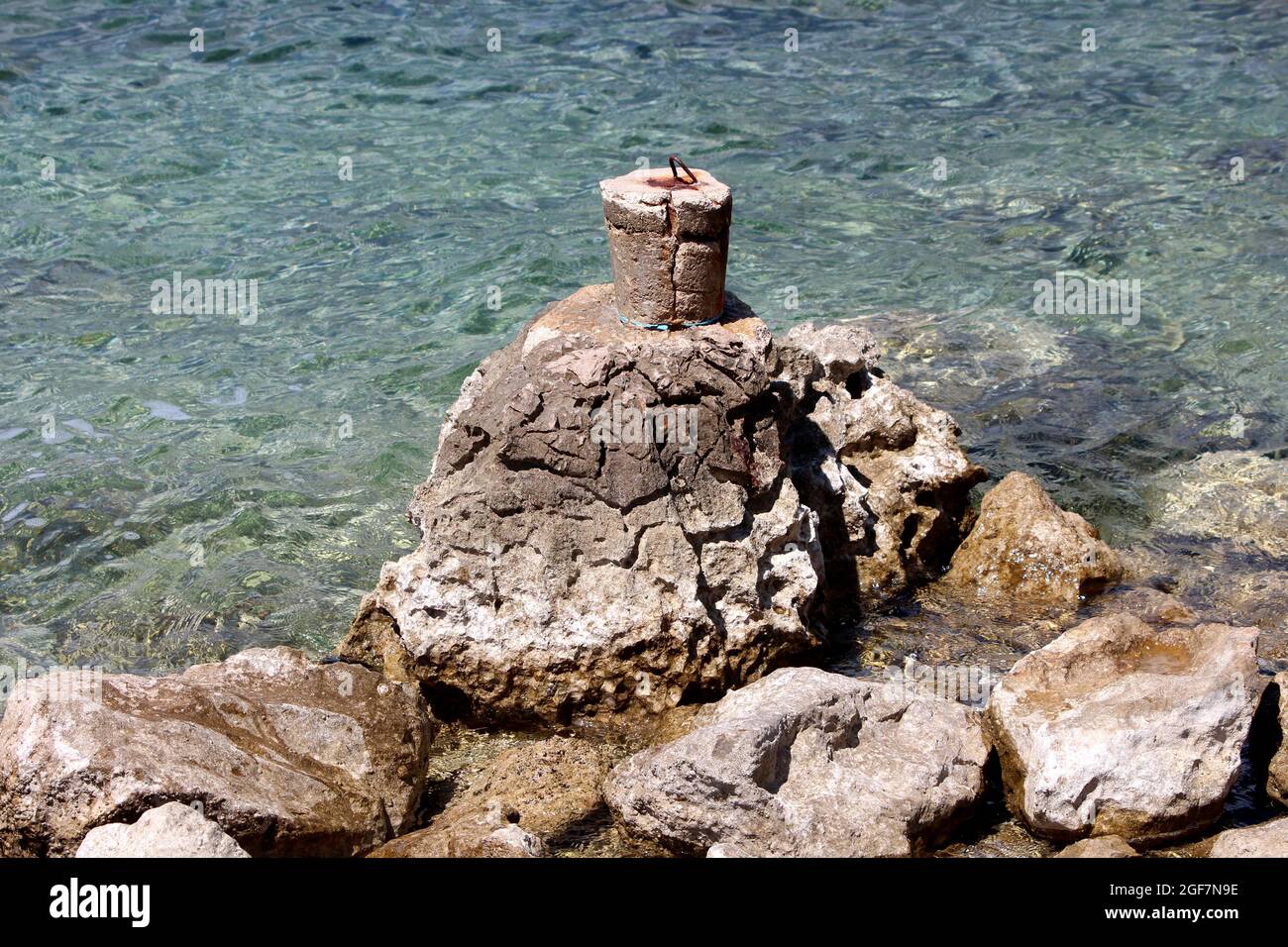 Improvised homemade stone mooring bollard with rusted metal hook on top ...