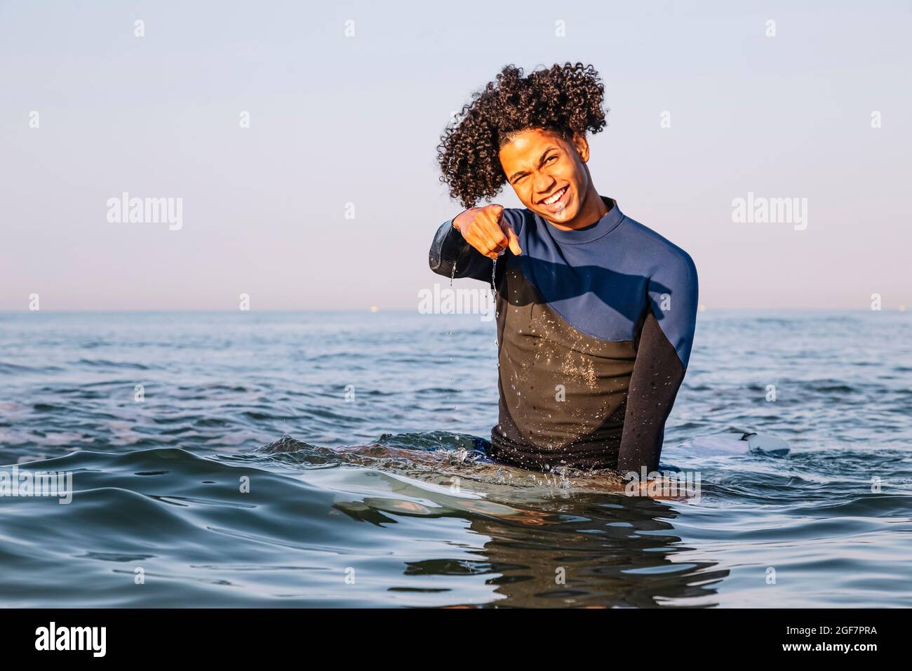 Surfer with afro hair sitting on his surfboard in the ocean water ...