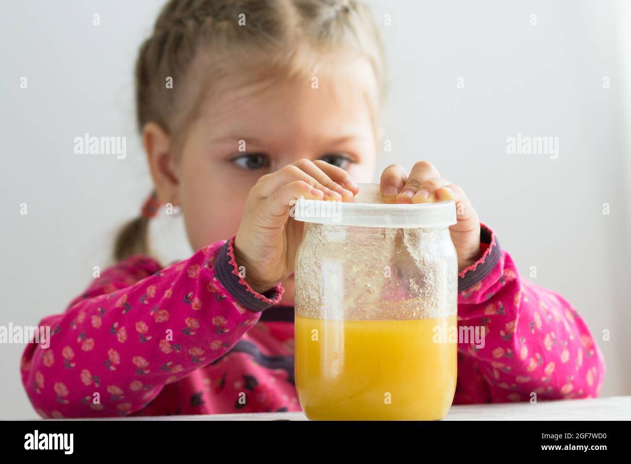 Caucasian child of three years old trying to pull off cover from jar ...