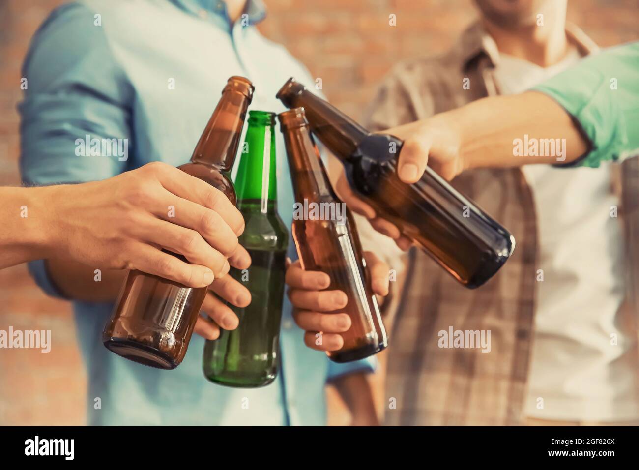Male group clinking glass bottles of beer on brick wall background ...