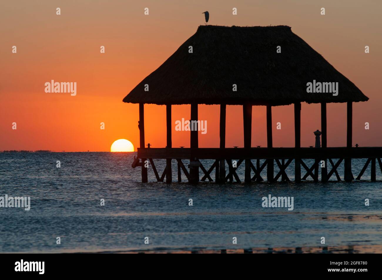 Wooden pier by the sea with thatched roof at sunset on a tropical beach ...