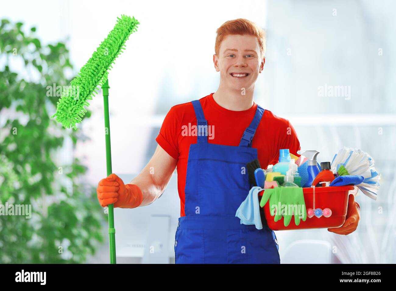 Young janitor holding cleaning products and tools in office Stock Photo ...
