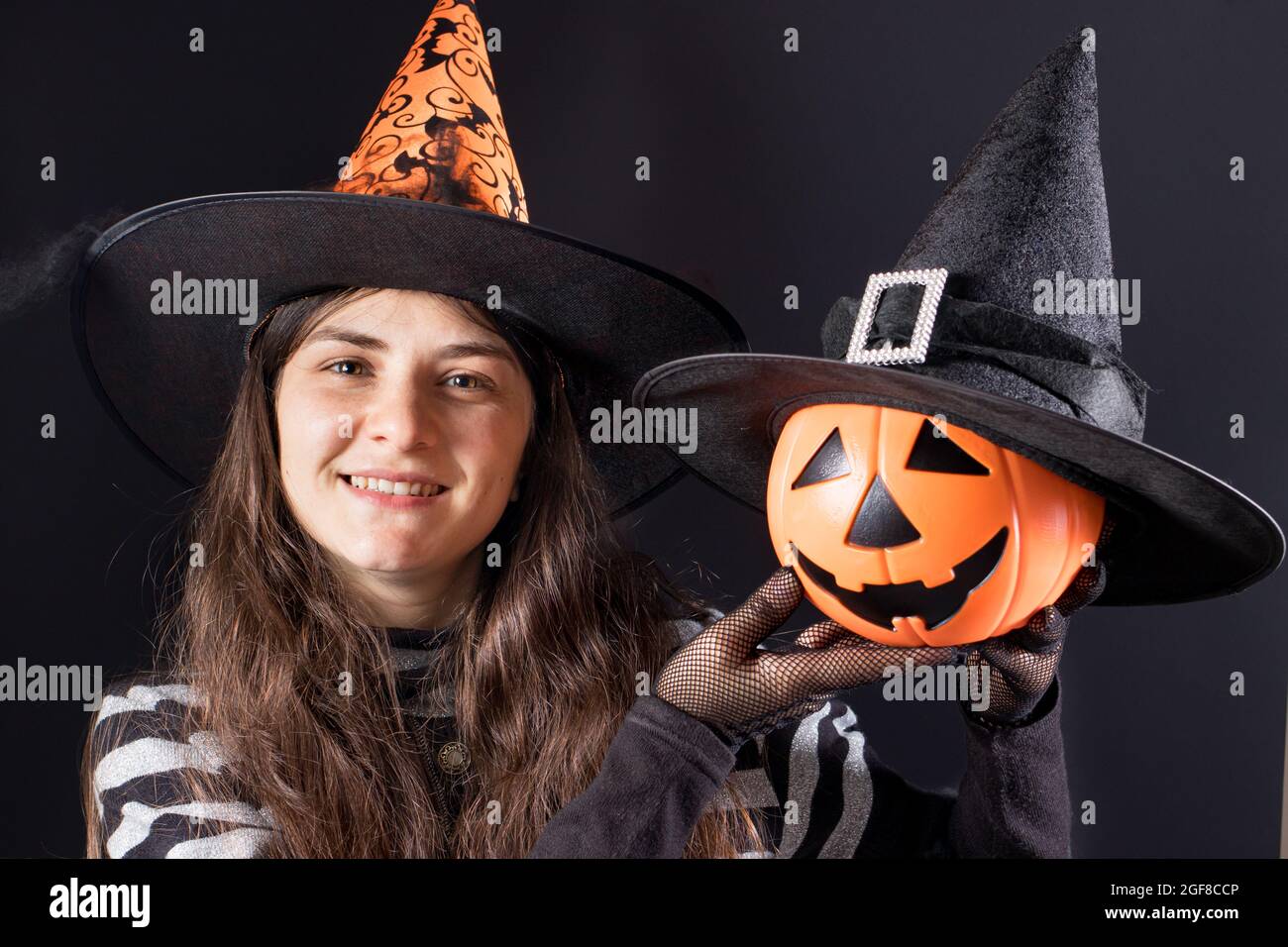 A woman in a witch costume in an orange hat holds a pumpkin lantern ...