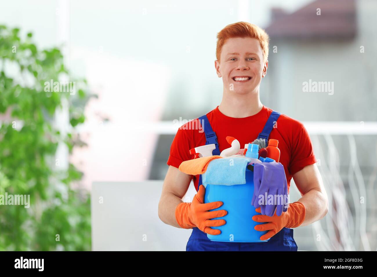 Young janitor holding cleaning products and tools on bucket in office ...
