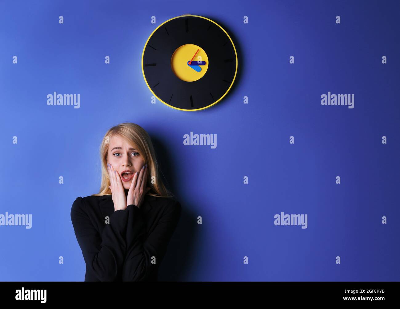 Young attractive woman under the clock, on blue background Stock Photo ...