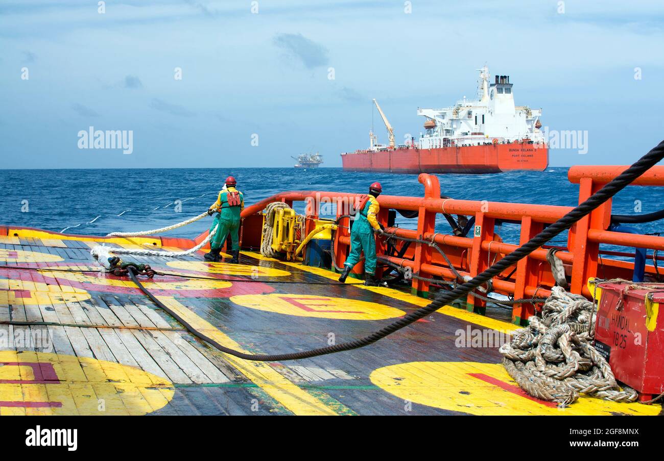 two skilled marine crew connecting cargo hose from FPSO to crude oil tanker at middle at sea ...