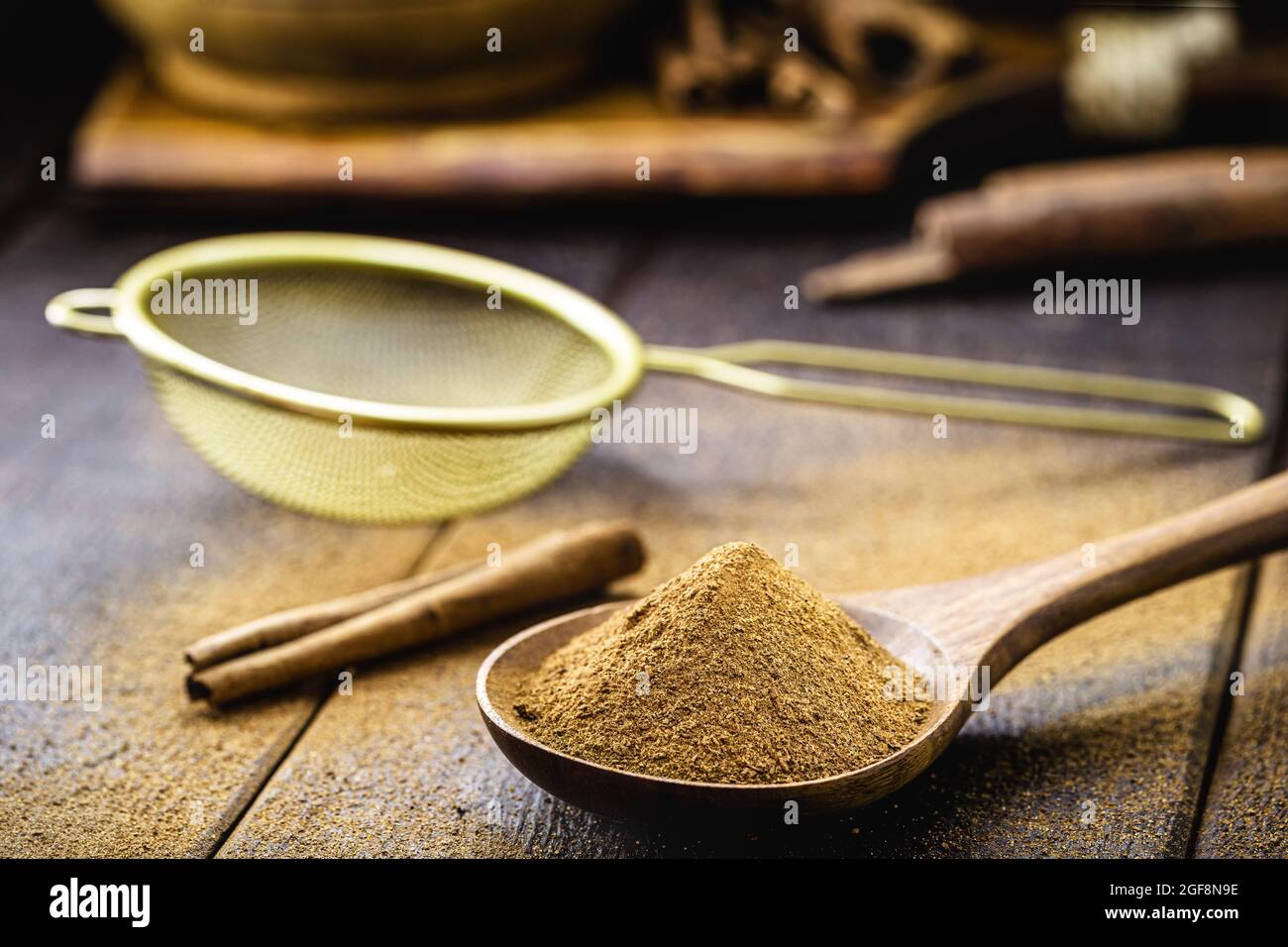 Powdered and unpeeled cinnamon with spoon and sieve, sprinkled on table ...