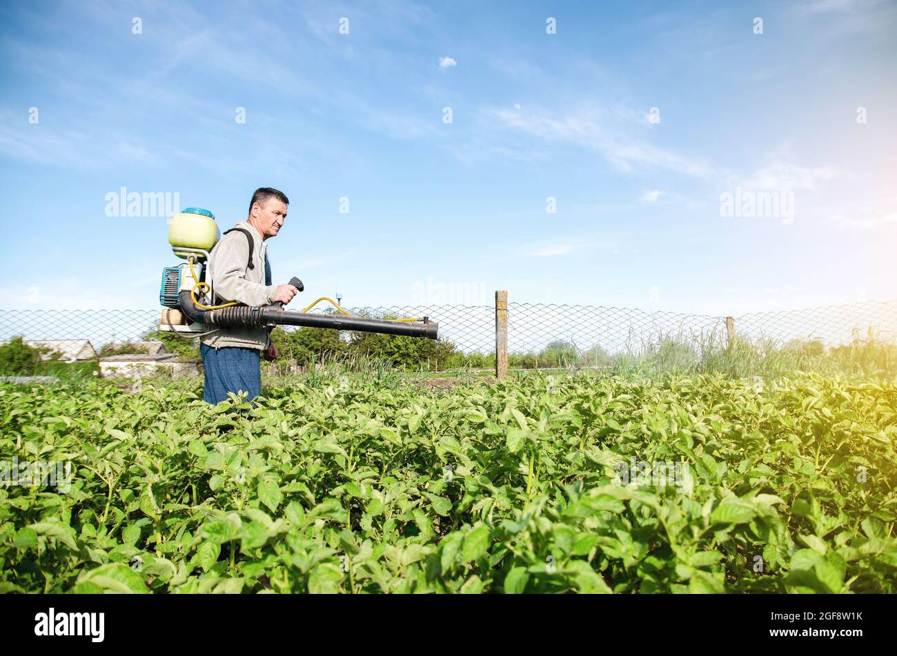 A farmer with a pesticide sprayer machine walks across the field ...