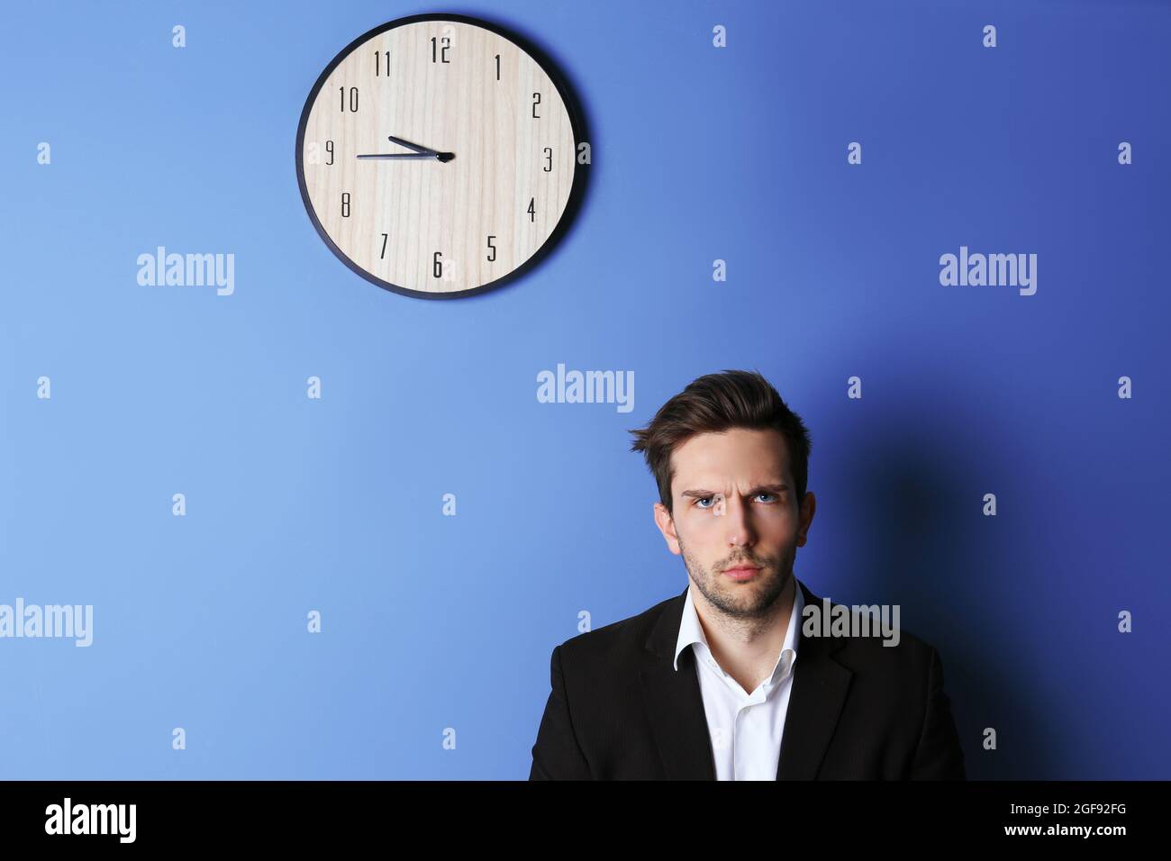 Man in black suit standing beside a big clock on blue wall Stock Photo ...
