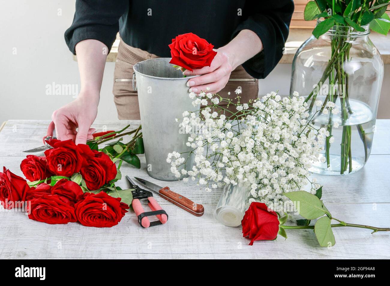 Florist at work: woman arranging bouquet of red roses in silver vase ...
