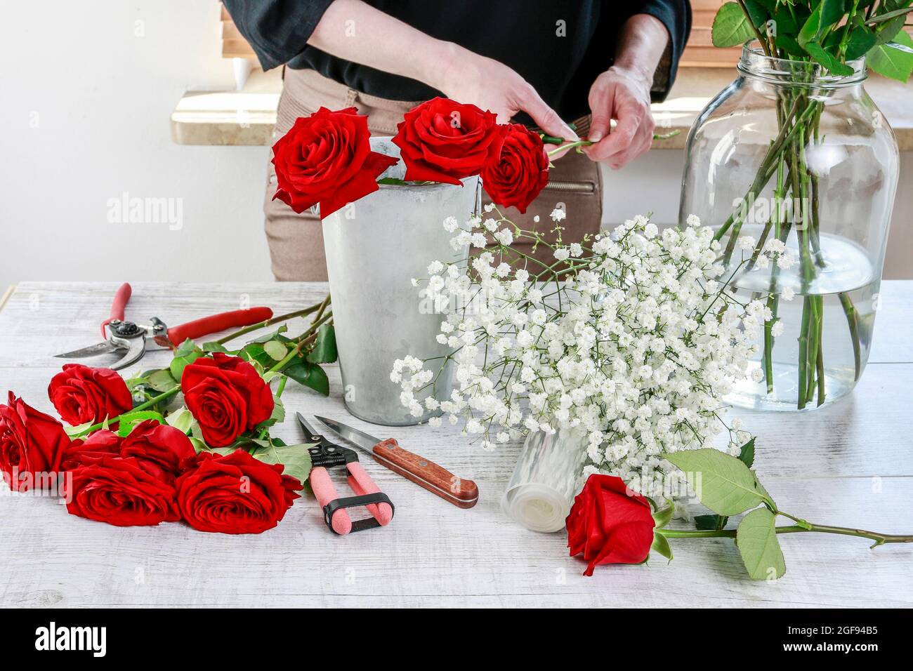 Florist at work: woman arranging bouquet of red roses in silver vase ...