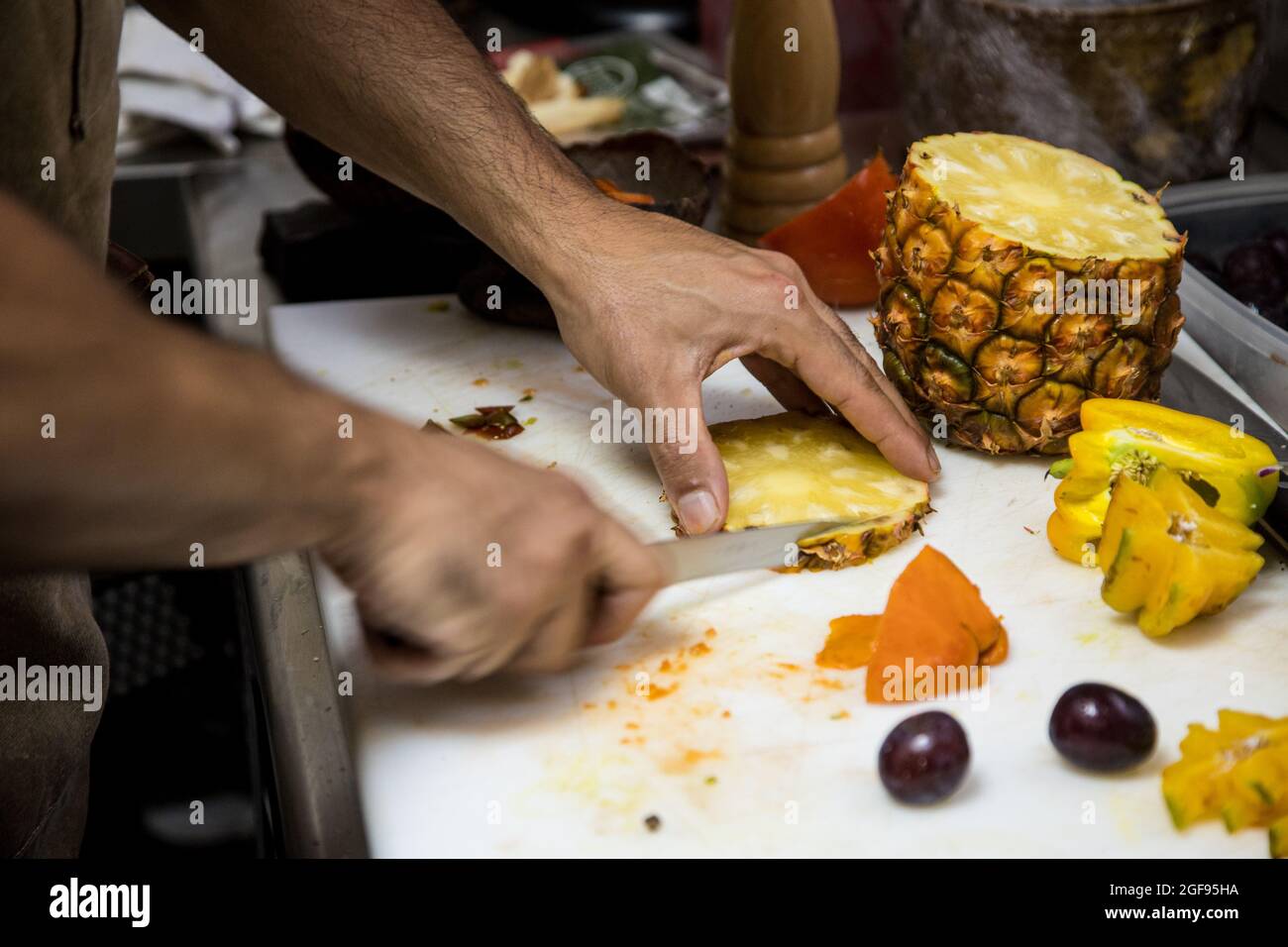 Shot of a man slicing a pineapple on a white kitchen table with a sharp ...