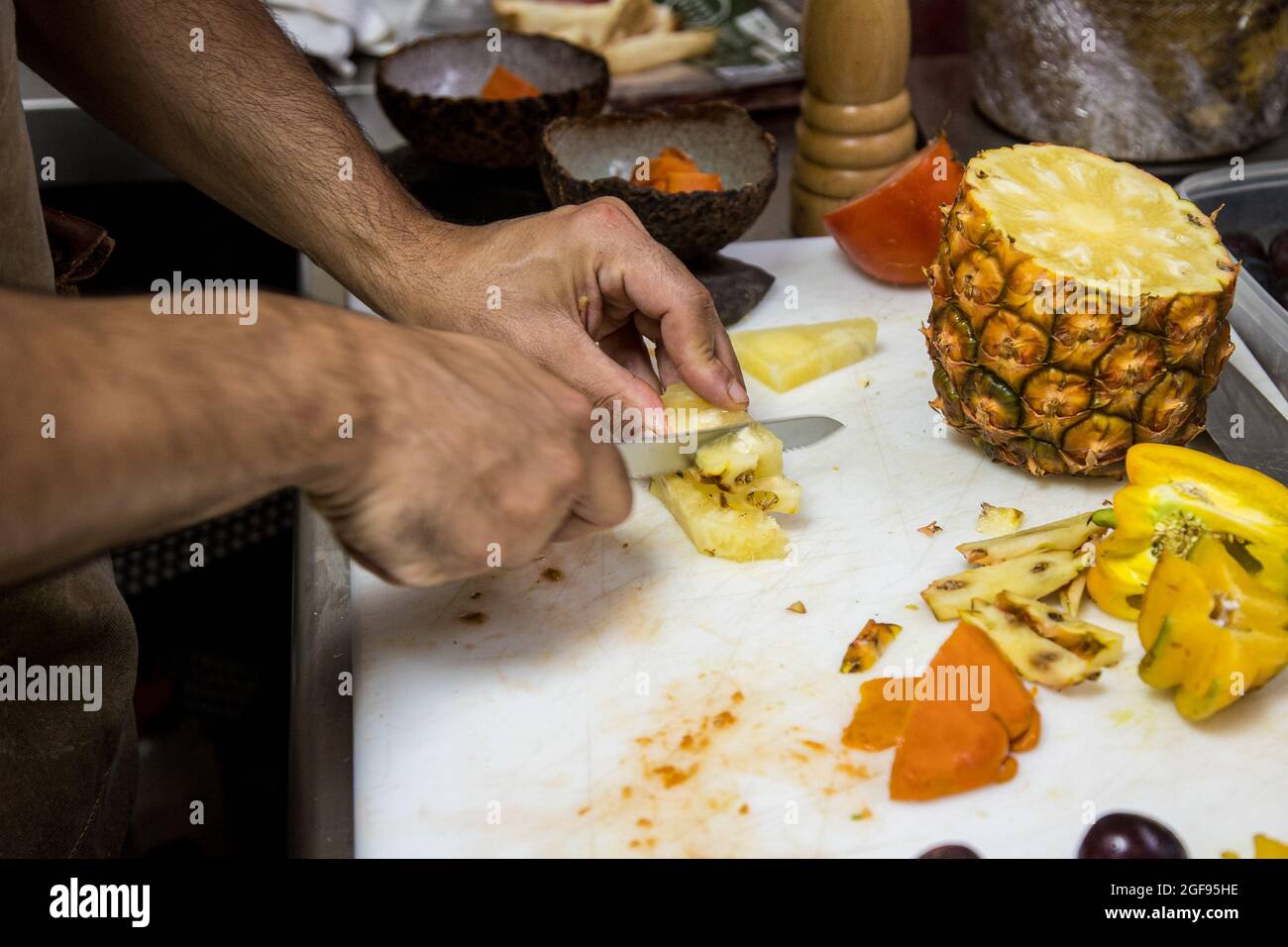 Shot of a man slicing a pineapple with a sharp knife on a white kitchen ...