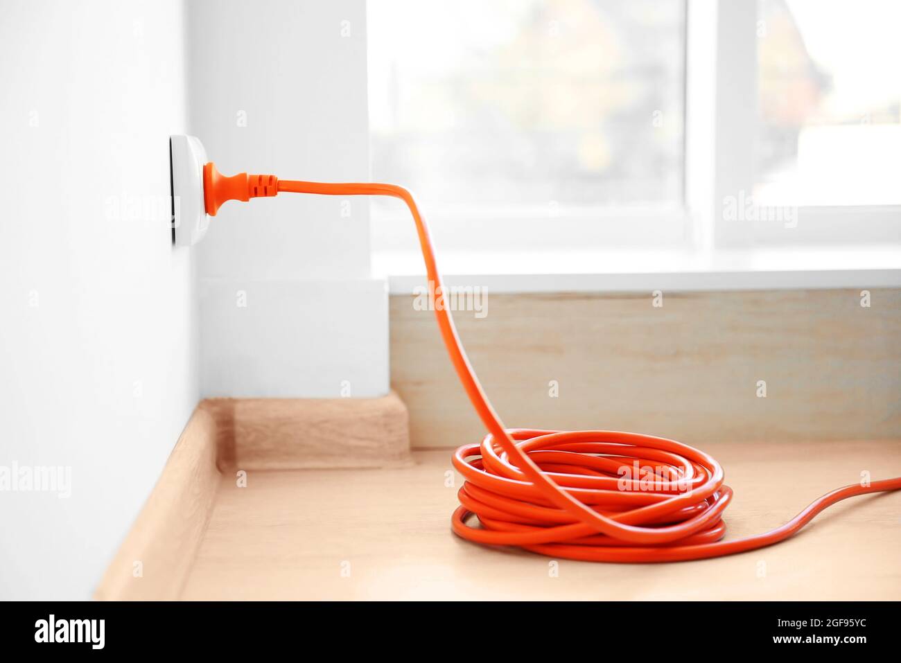 Orange extension into power outlet indoors Stock Photo - Alamy