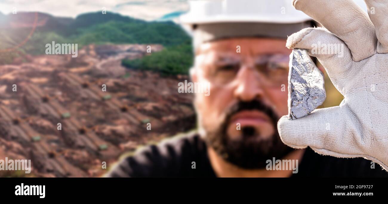 man miner holding silver stone, in the background a large open pit ...