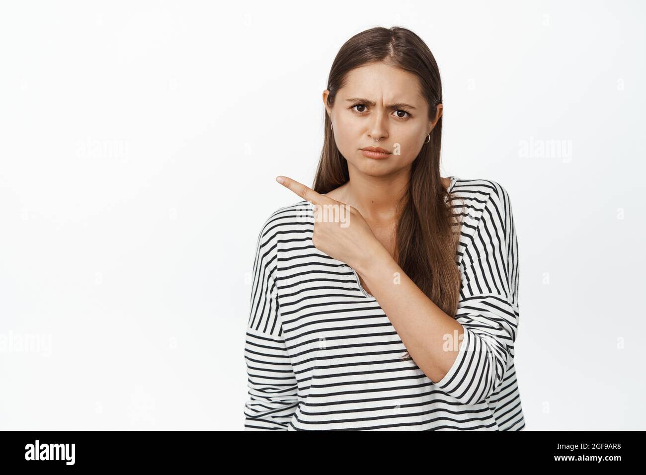 Disappointed girl pointing finger at upper left corner, showing smth ...