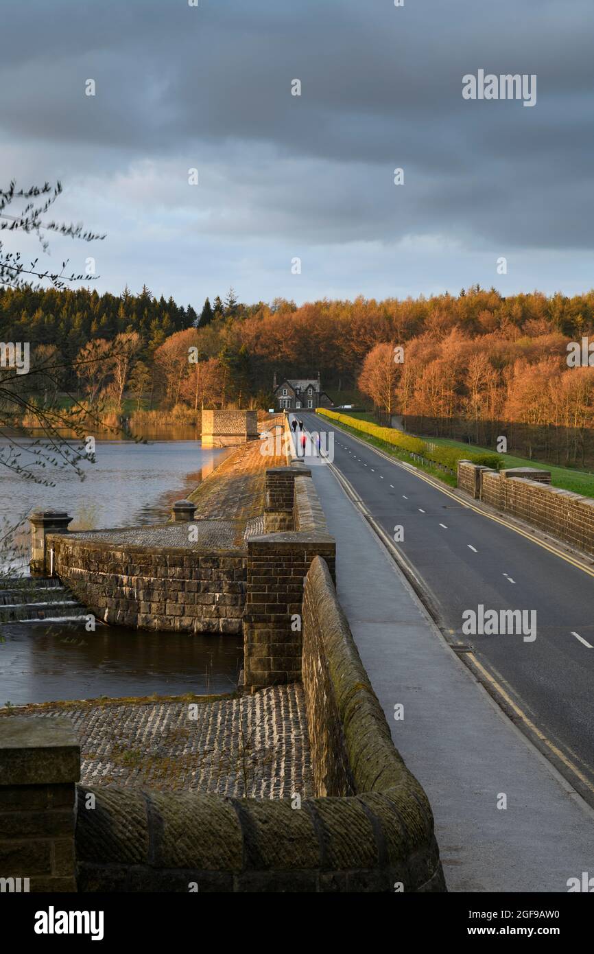 Dam embankment wall, walkers by road, autumnal woodland colours, dark ...
