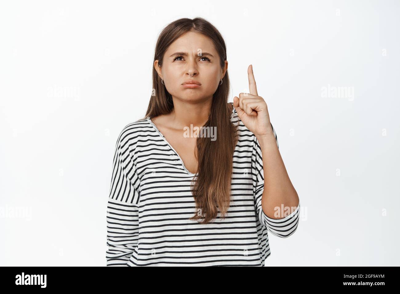 Suspicious young woman pointing finger up and looking at advertisement ...
