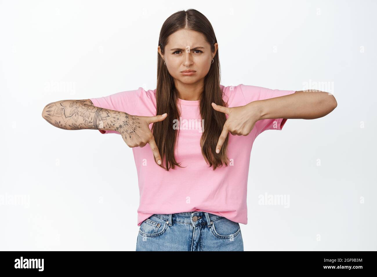 Sad grimacing girl pointing fingers down, furrow eyebrows from smth ...