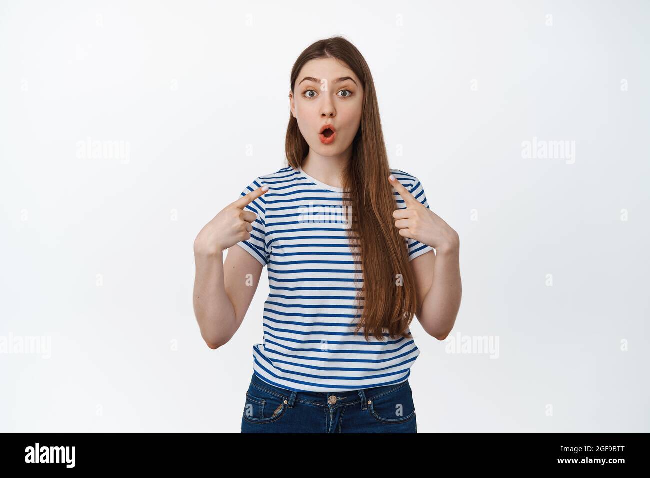 Portrait of girl gasp in awe, look surprised and pointing at herself ...