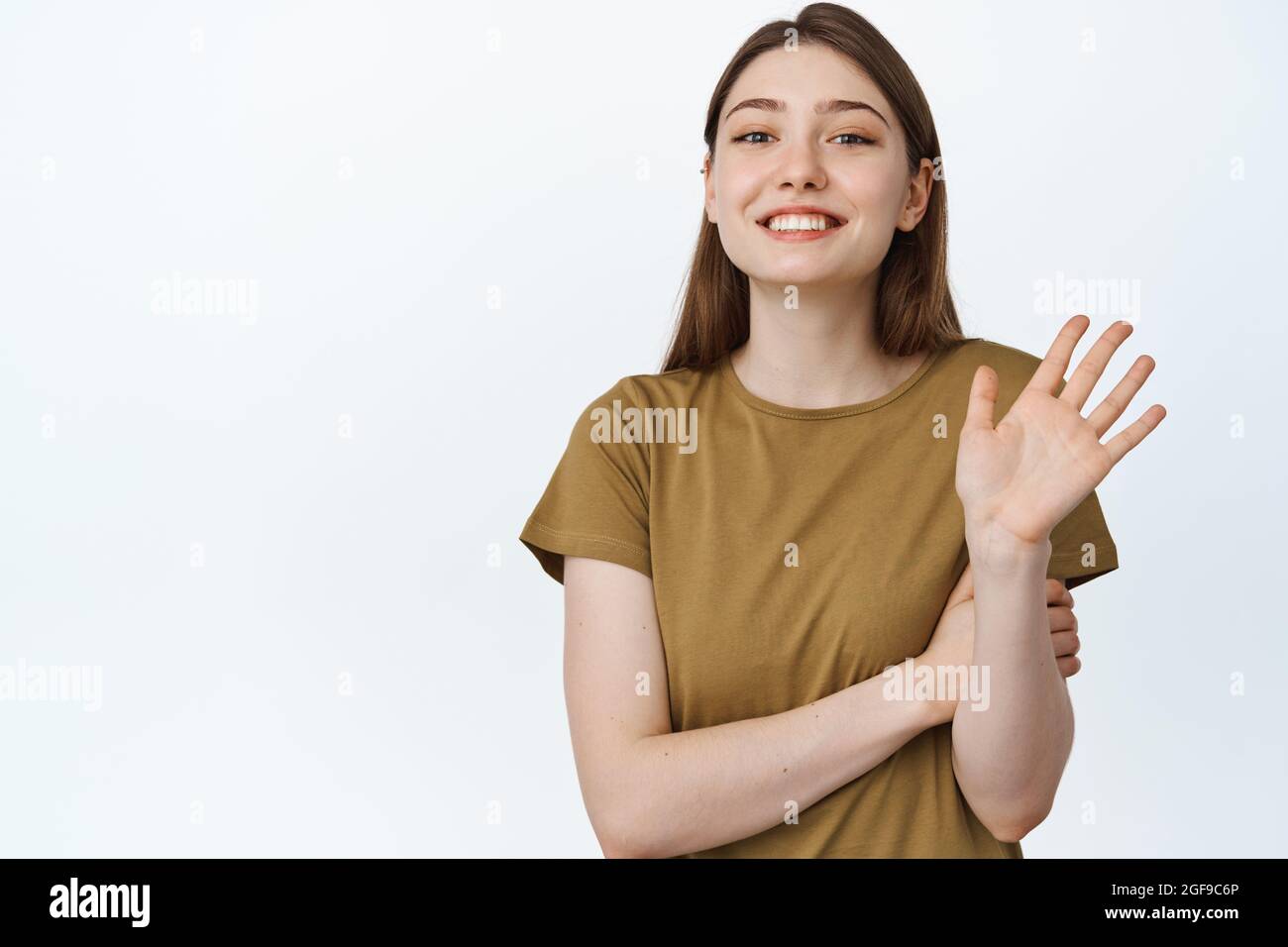 Friendly girl waving raised hand, greeting gesture, smiling happy at ...