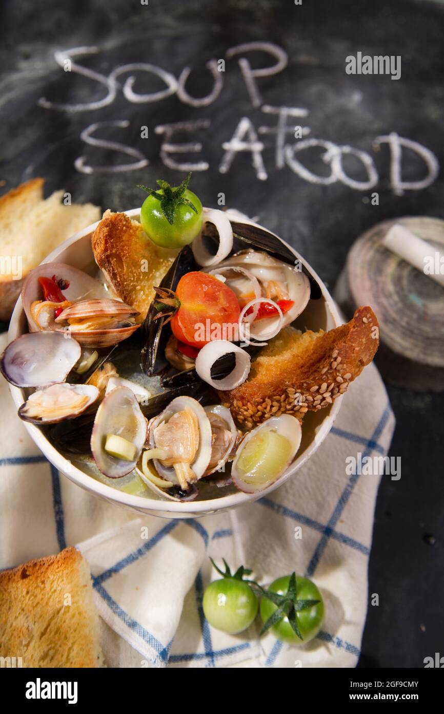 Presentation of a soup with seafood on a black background with writing ...