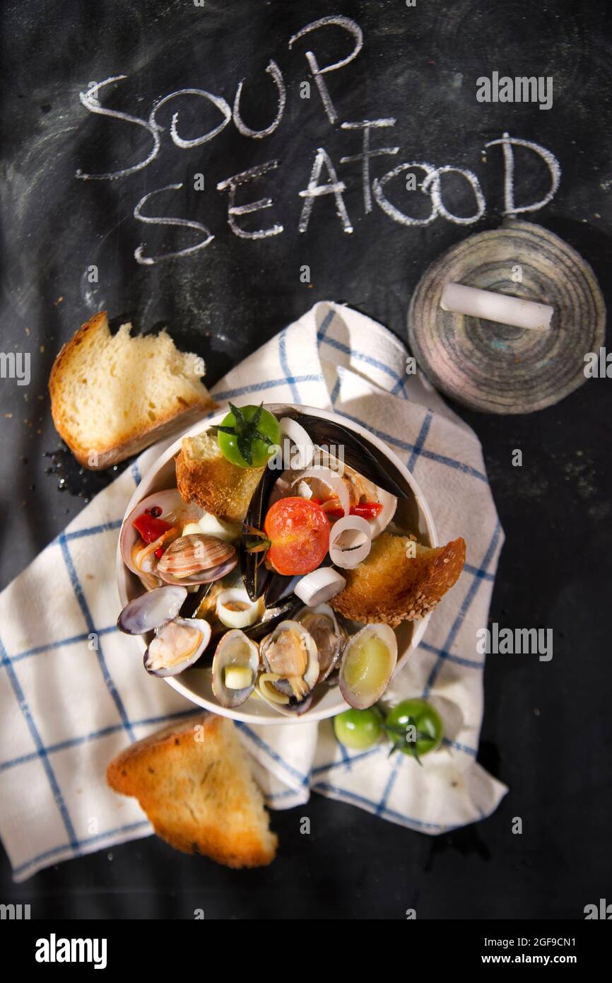 Presentation of a soup with seafood on a black background with writing ...